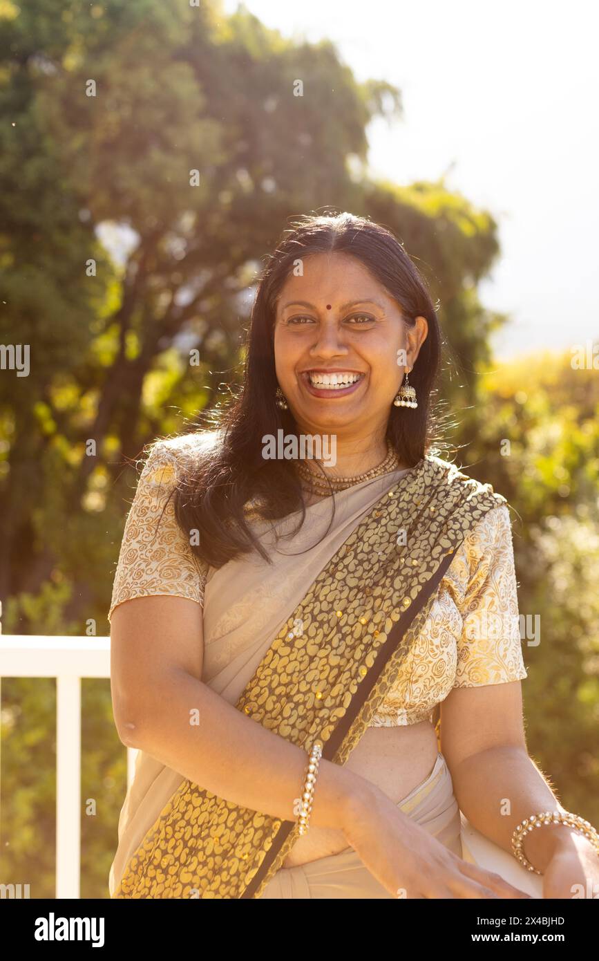Indian woman wearing sari standing outside, laughing. She has dark hair ...