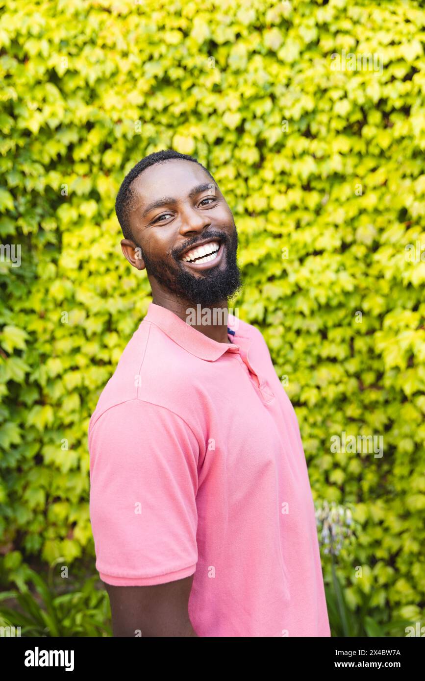 African American man standing outdoors, smiling in front of green ...