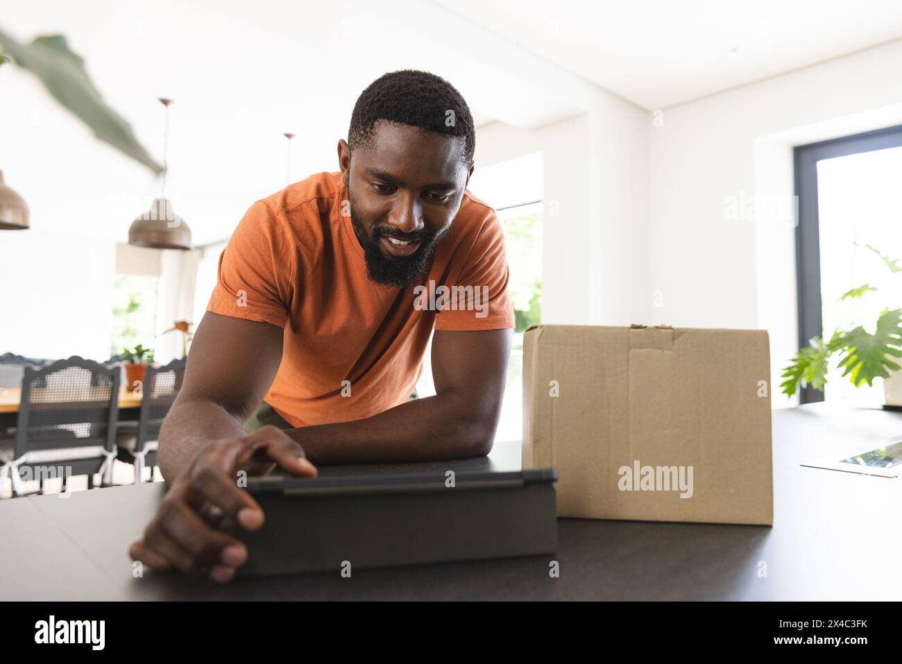 African American male homeowner opening cardboard box at home. Wearing ...