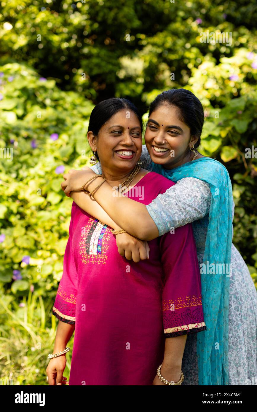 Indian mother and teenage daughter, both with dark hair, hugging outdoors. Wearing pink kurta ...