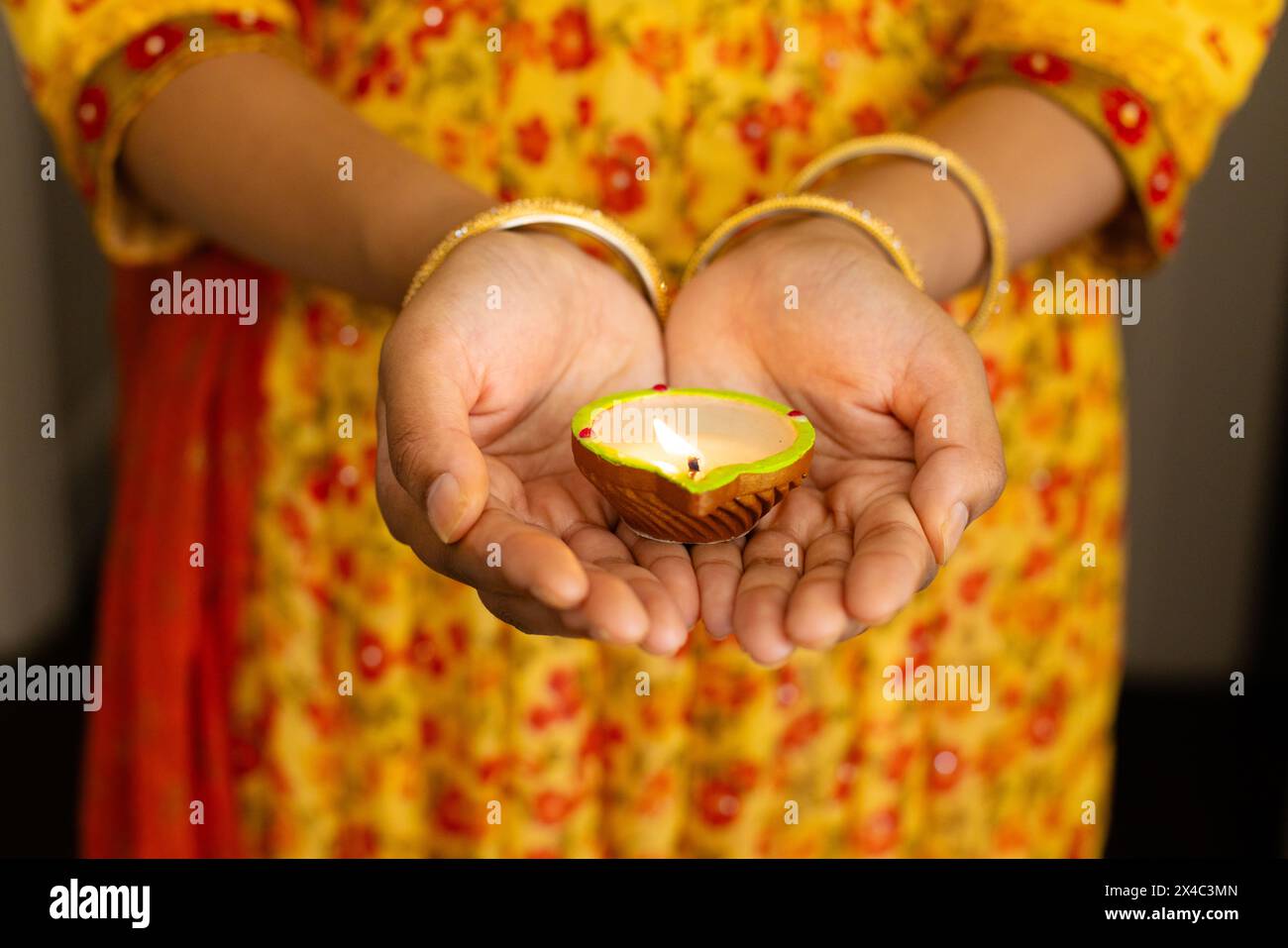 Indian young woman holding lit candle, wearing yellow traditional ...