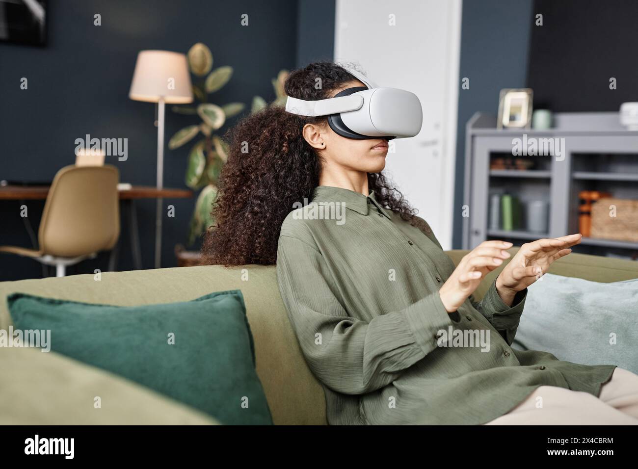 Medium shot of young biracial woman with curly hair wearing VR headset ...