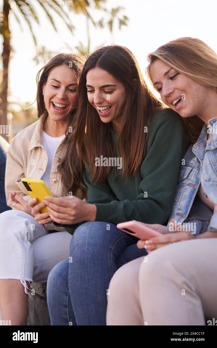 Group of gen z beautiful female friends smiling sitting outdoors using ...