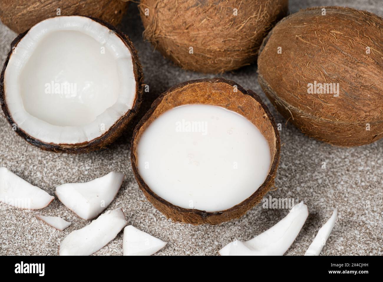 Coconut milk in coconut shell and half coconut, chopped flesh on grey ...
