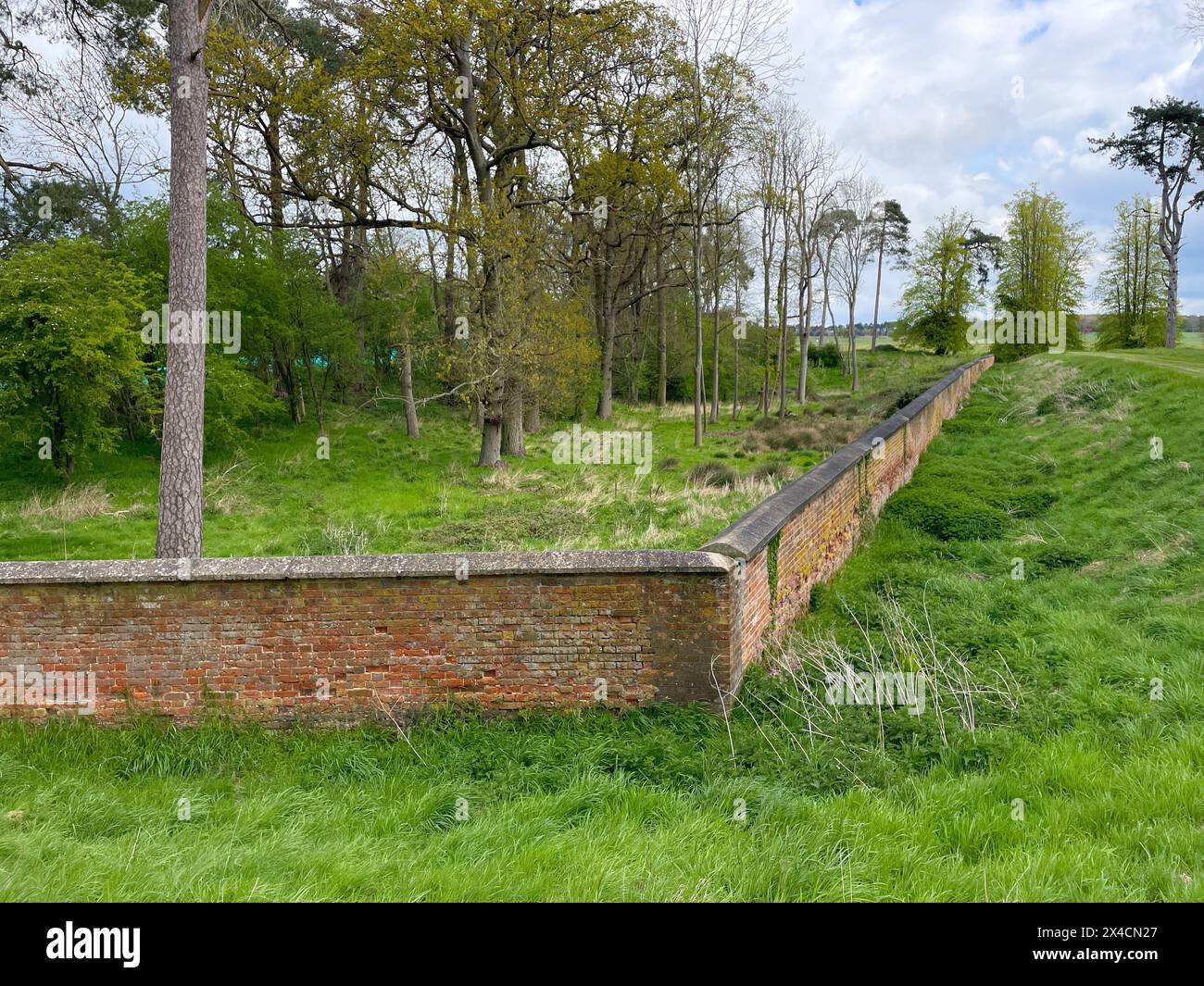 A brick wall forms a corner boundary of an estate with trees and grass ...