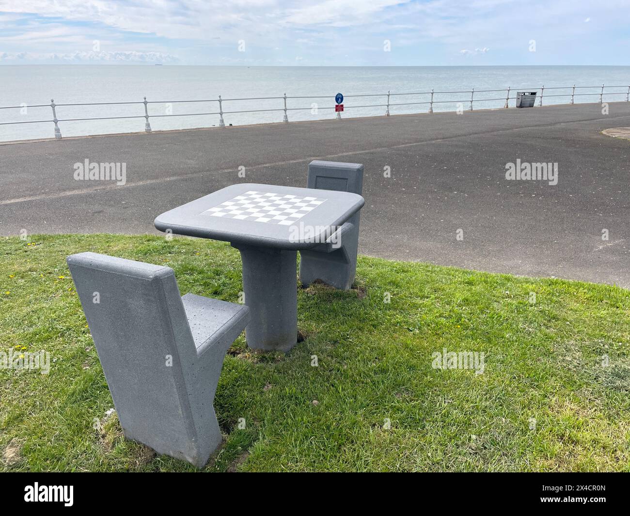 Two seats and a table with a chess board printed on top by a seaside ...