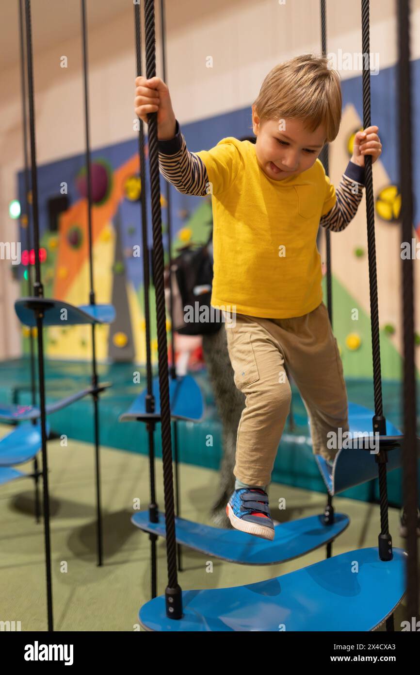 A young boy is hanging from a rope and balancing on a blue platform ...