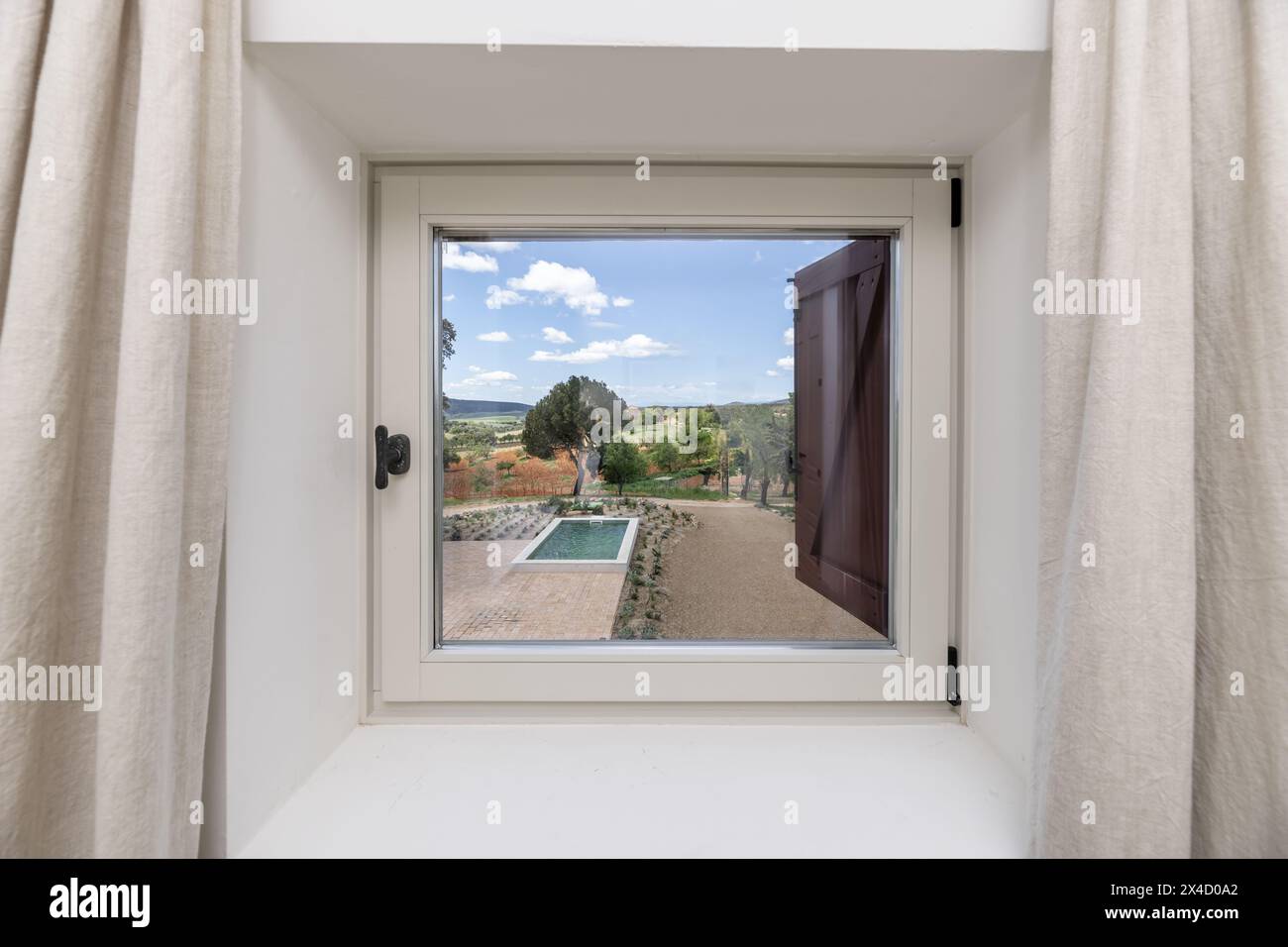 A room with a square window overlooking a field with a swimming pool ...