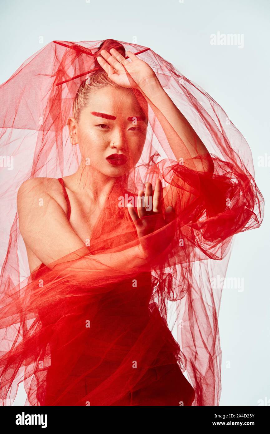 An attractive Asian woman poses in a vibrant red dress and a veil over ...