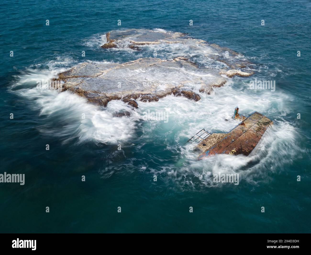 A shipwreck resting on a rock half submerged from a drone view Stock ...