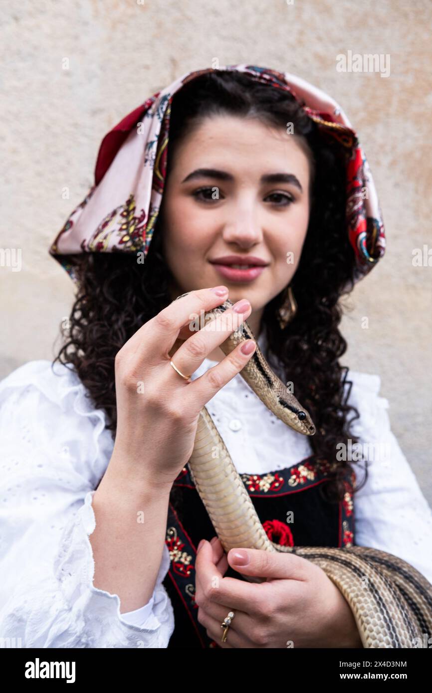 A young lady dressed in regional costume shows the snake that she will ...