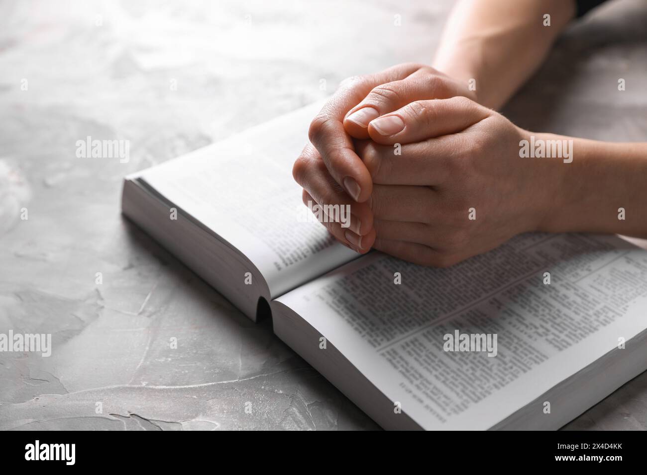 Religion. Christian woman praying over Bible at gray textured table ...