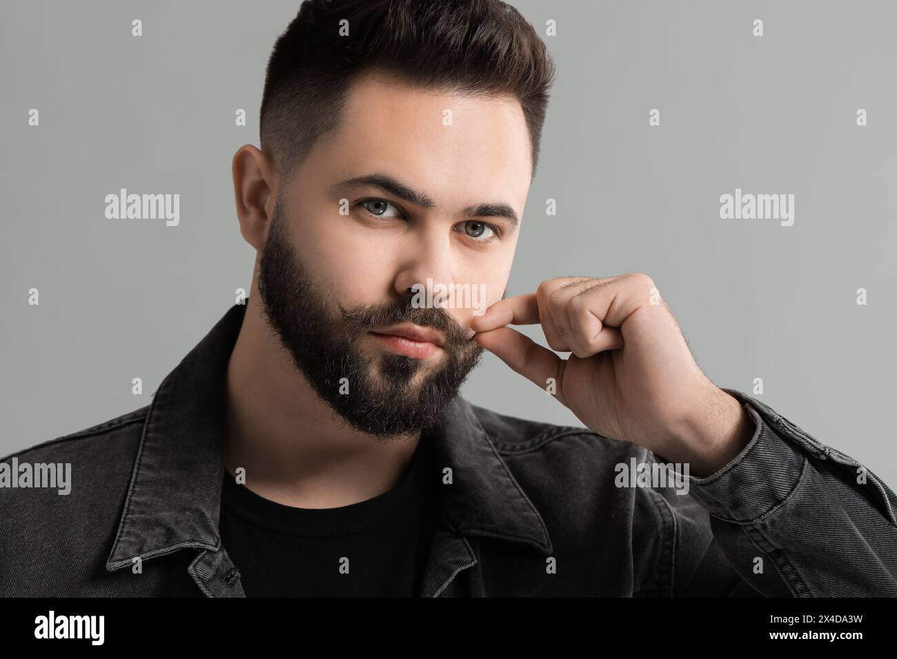Young man touching mustache on grey background Stock Photo - Alamy
