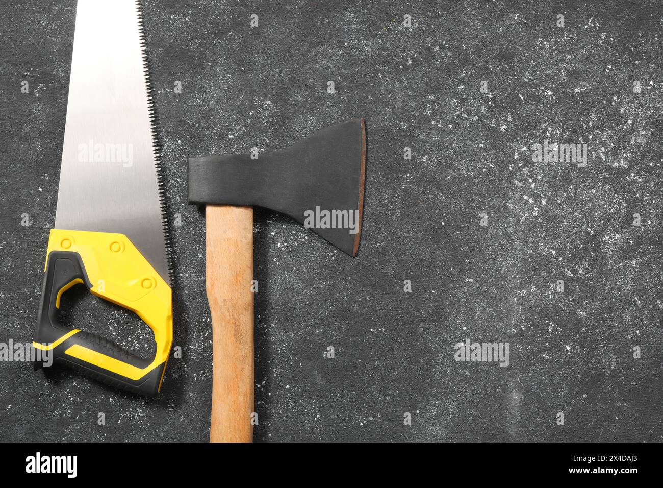 Saw with yellow handle and axe on dark gray textured background, flat ...