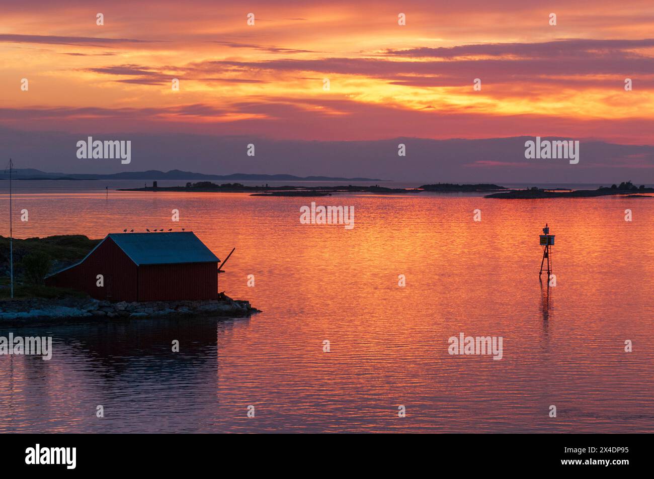 A fiery sunset sky beyond silhouetted islands in the Norwegian Sea at ...