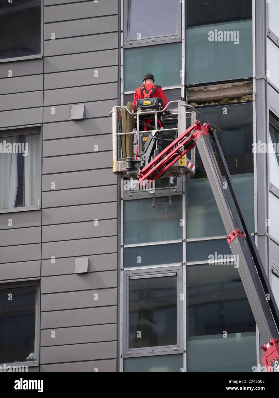 Worker in elevated cherry picker platform undertaking reactive repair ...