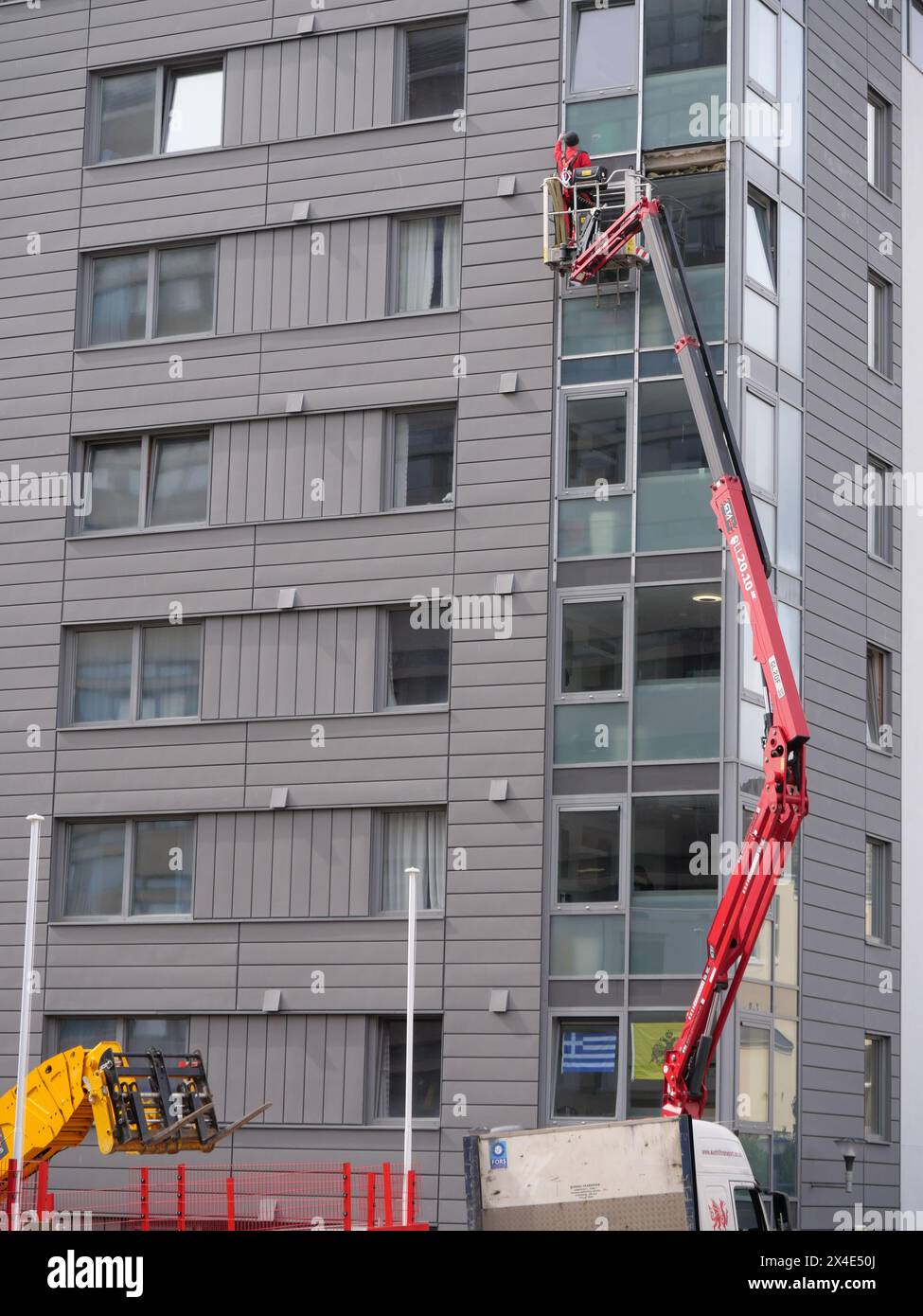 Worker in elevated cherry picker platform undertaking reactive repair ...