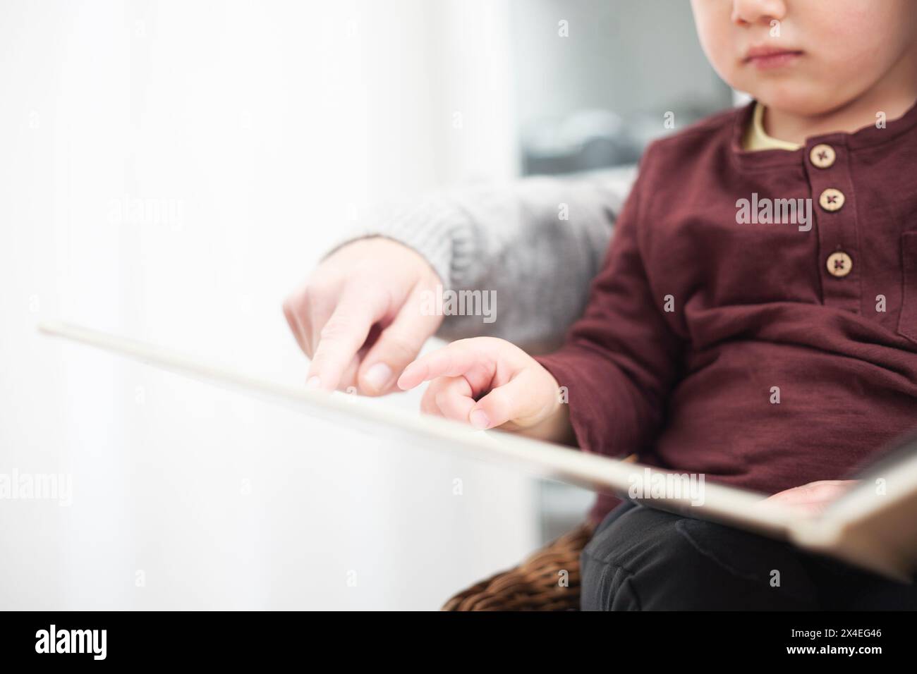 A child is sitting in a chair with a book in front of him. A person is ...