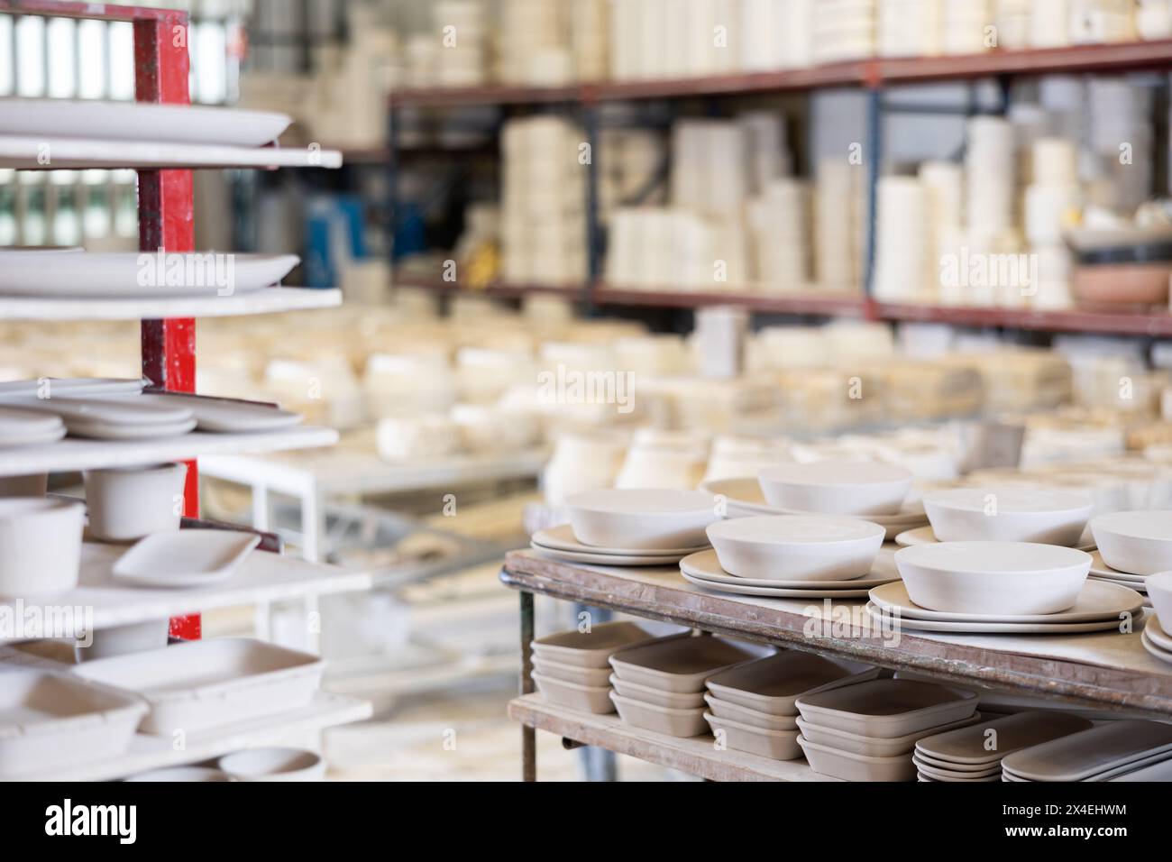 Unfinished ceramic bowls and plates organized on racks in pottery ...