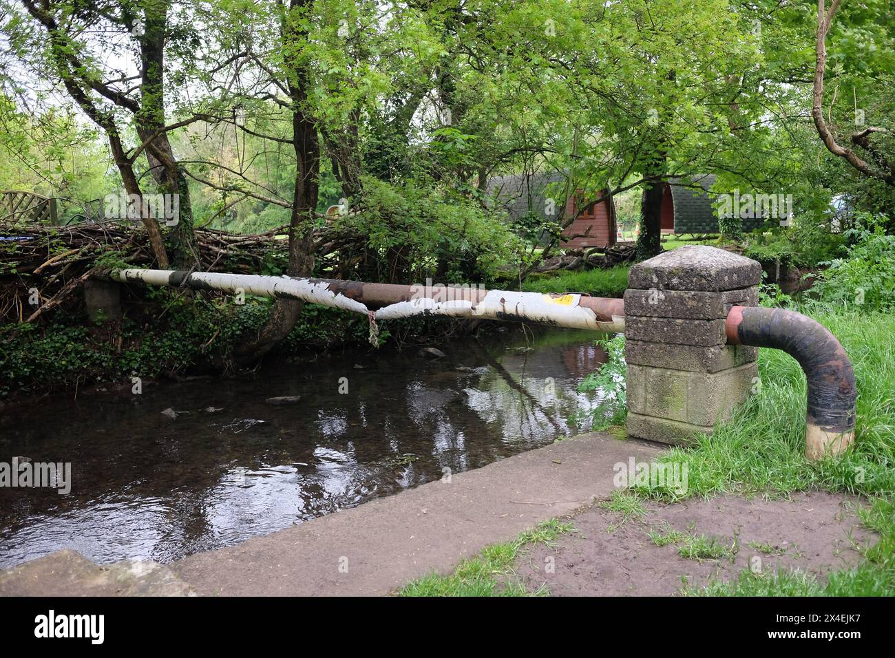 May 2024 - Old and tatty gas pipe crossing the river Yeo in the village ...