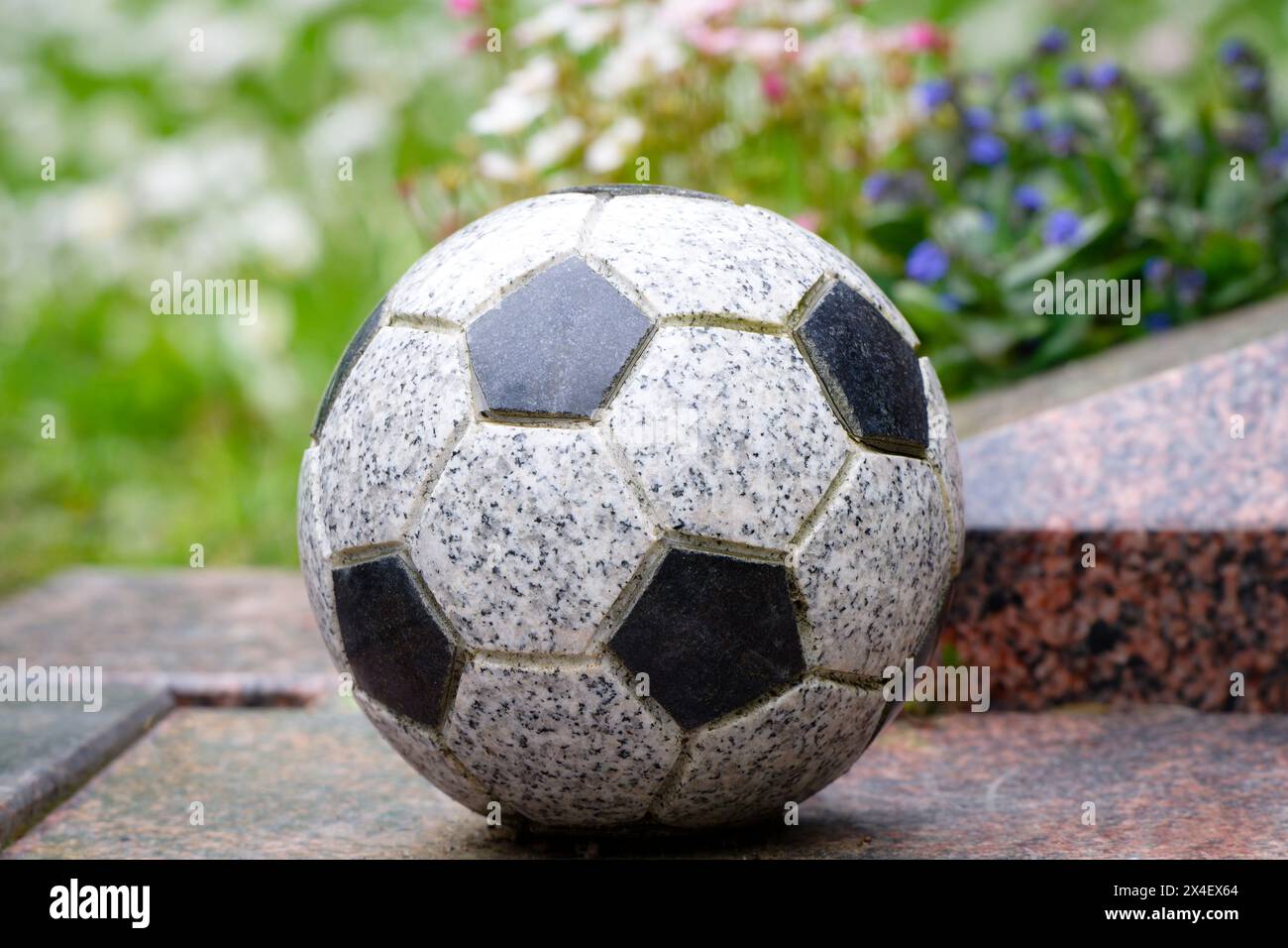 a stone football as decoration on a grave in front of colourful flowers ...