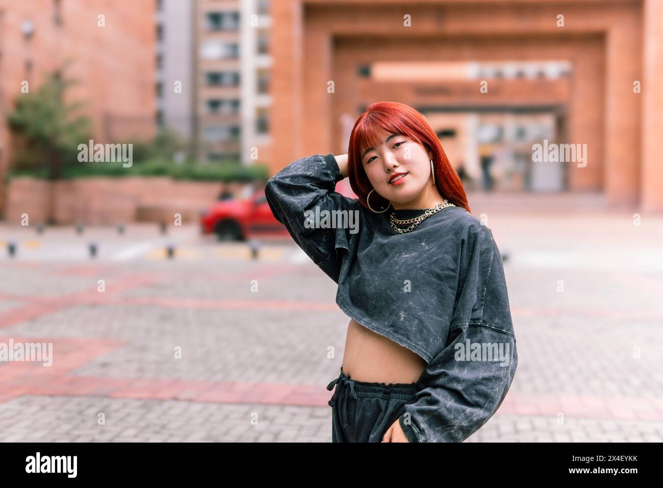 Confident Korean woman with striking red hair posing in a modern urban ...