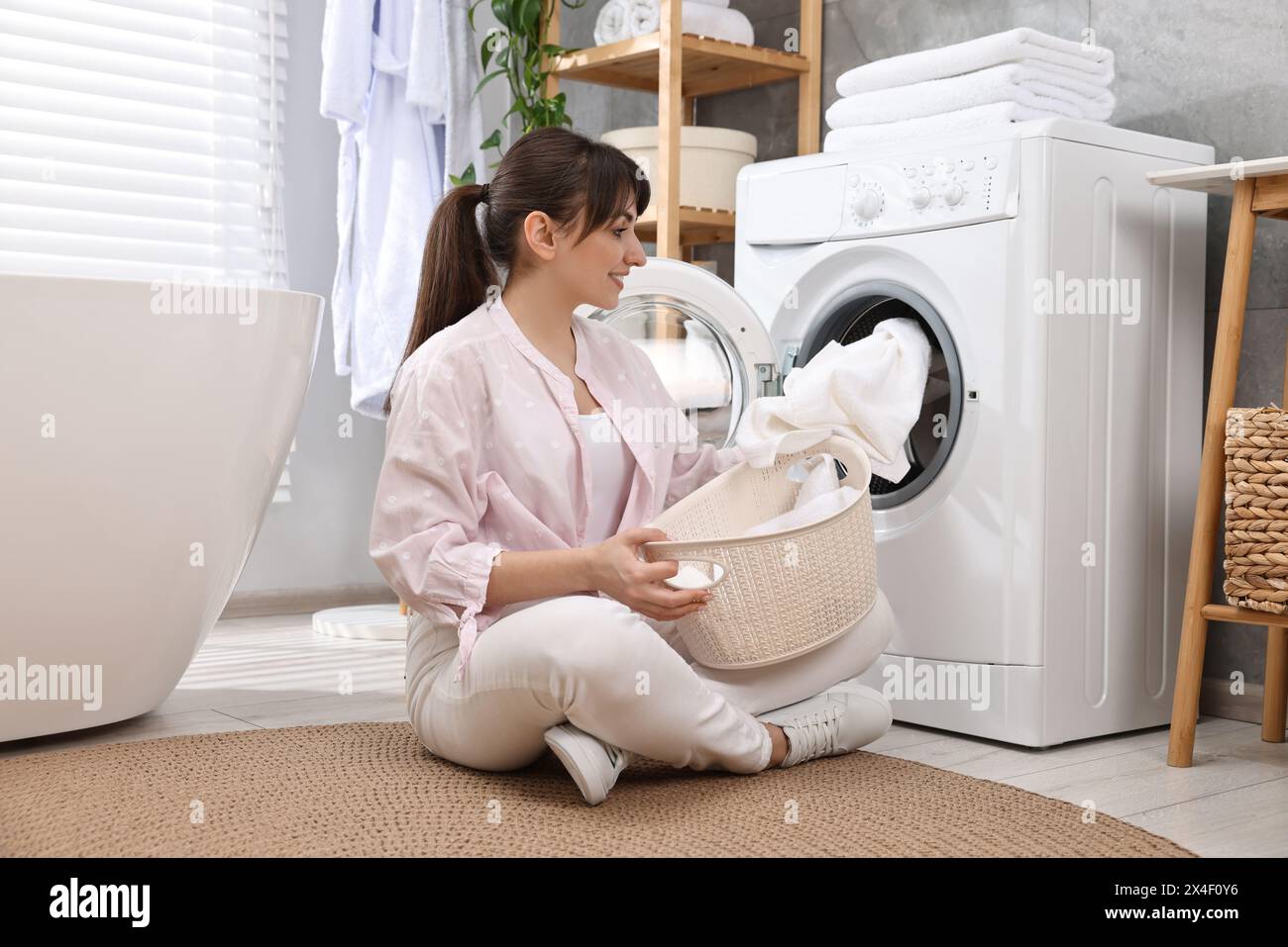 Happy young housewife putting laundry into washing machine at home ...