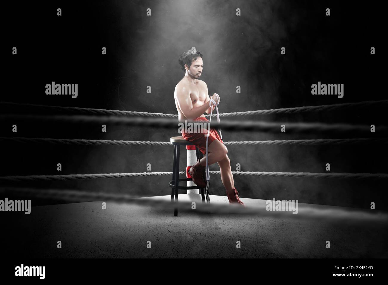 Portrait of a boxing man sitting and wrapping his hand with tape in the ...