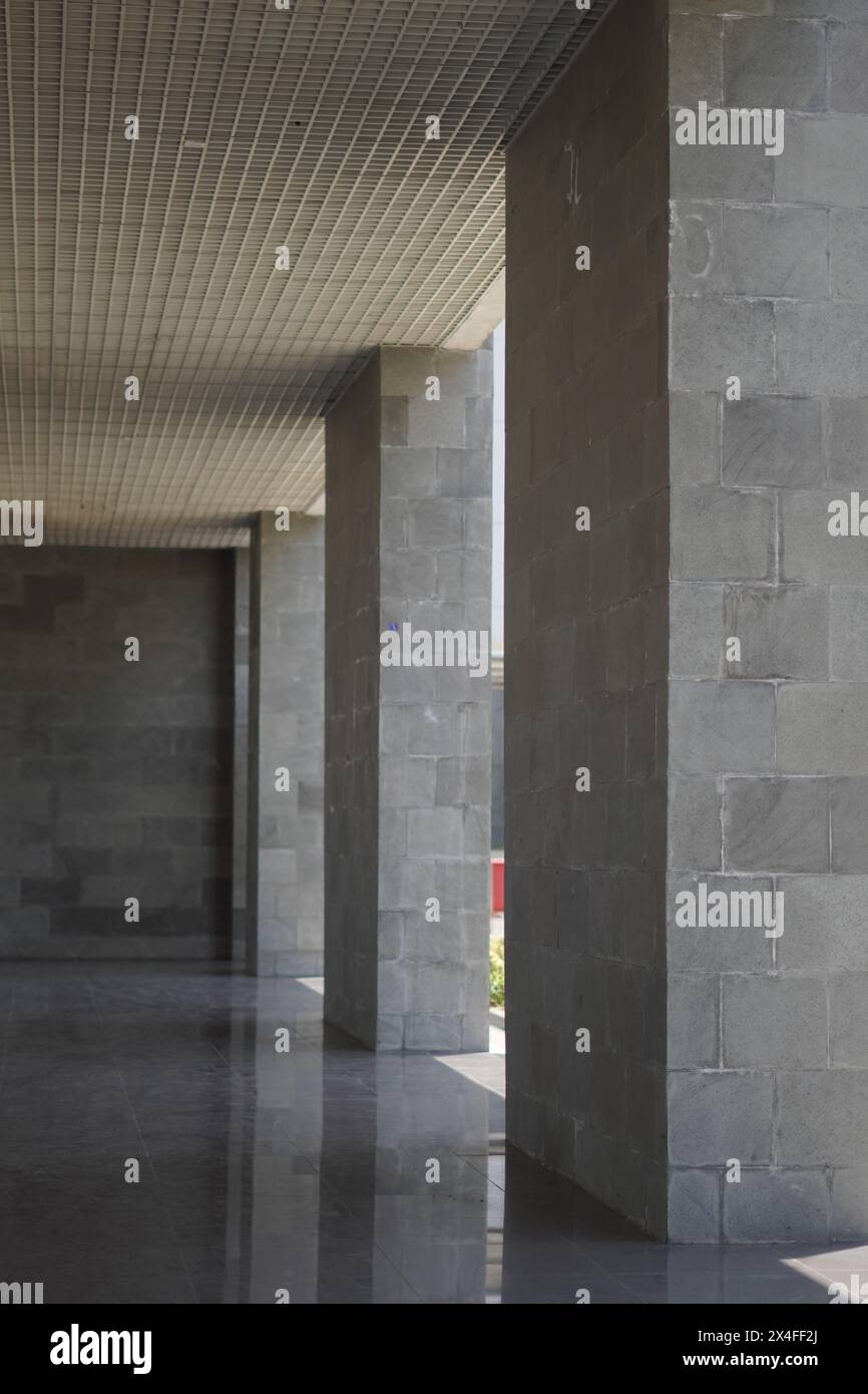 A dark hallway with gray square pillars with a light source from ...