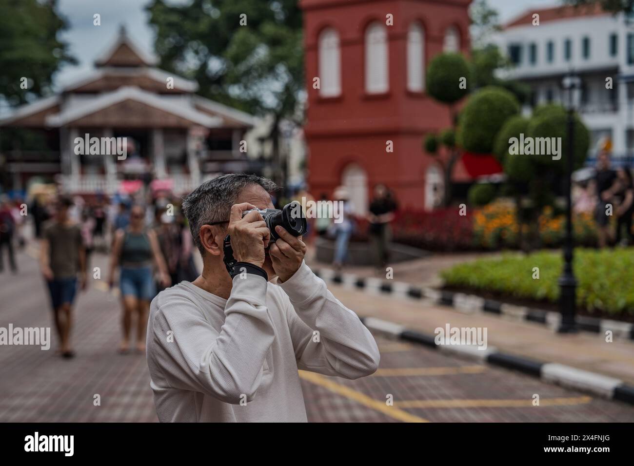 A focused elderly man capturing moments with his camera in a bustling ...