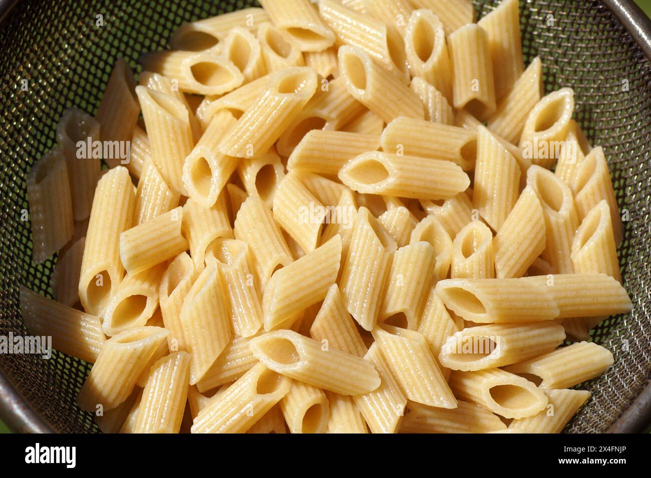 Close up cooked macaroni drained in a stainless steel sieve, strainer ...