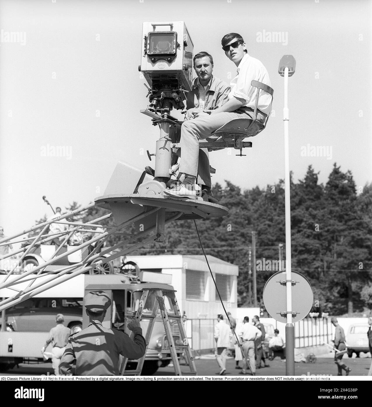 Filming in 1963. A cinematographer and his assistant sit on a moving ...