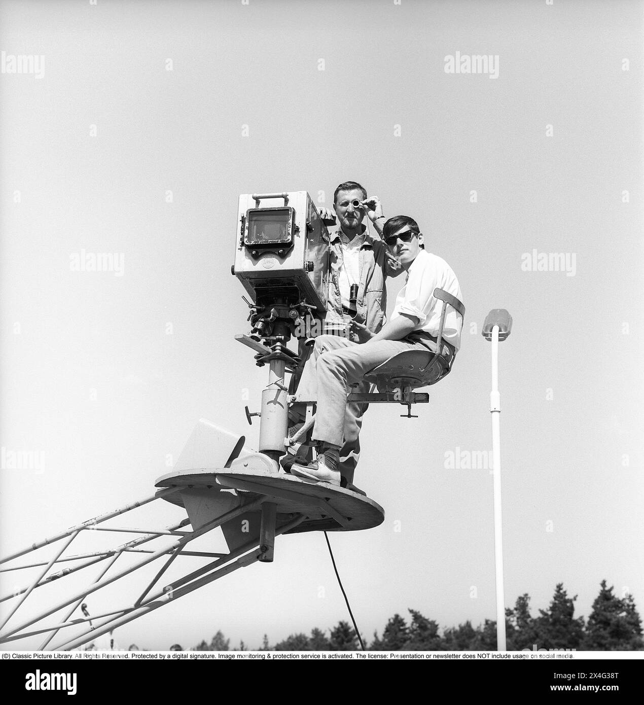 Filming in 1963. A cinematographer and his assistant sit on a moving ...