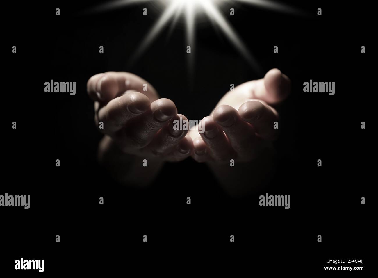 Christian woman holding hands under holy light in darkness, closeup ...