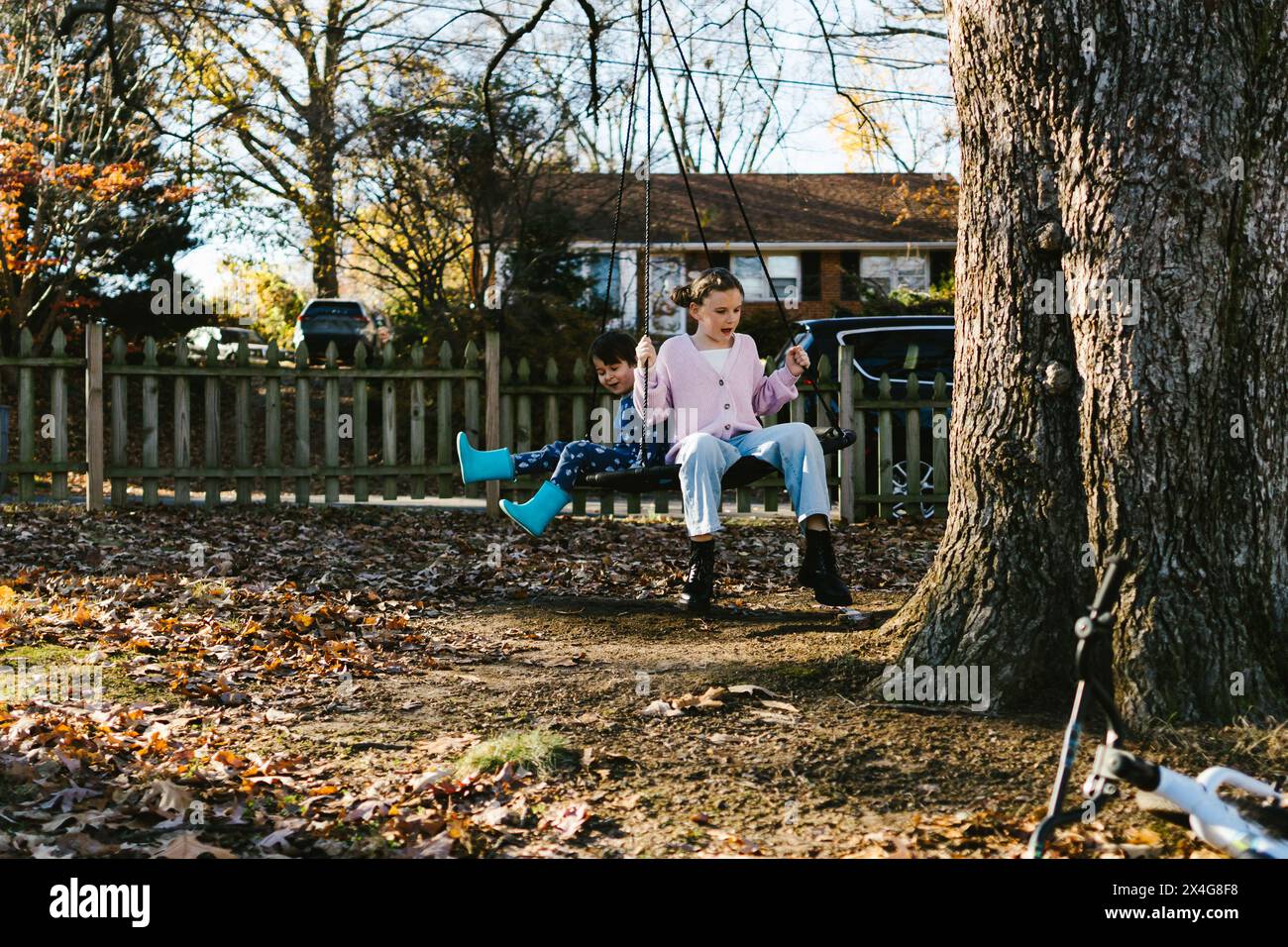 Kid cousins play on tree swing in fall in front yard neighborhood Stock ...