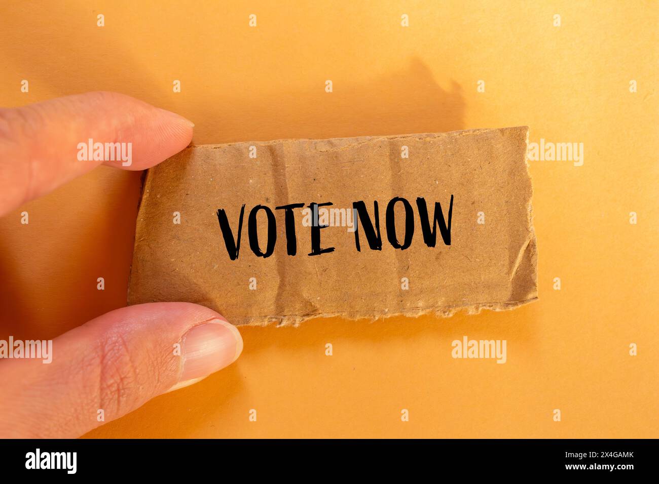 Vote now words written on ripped cardboard paper with orange background ...