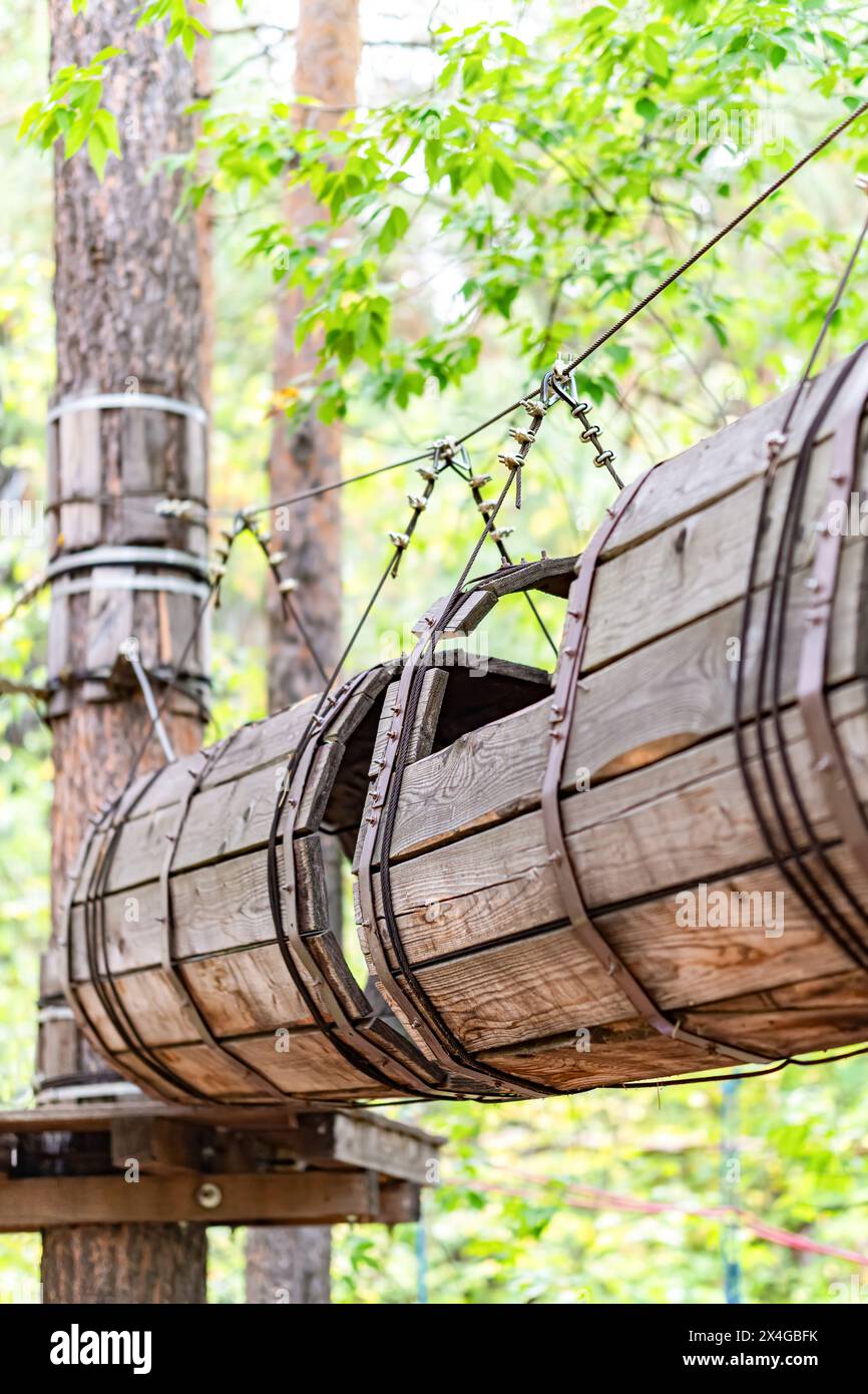 Wooden barrel tunnel obstacle suspended between trees, with cables and ...