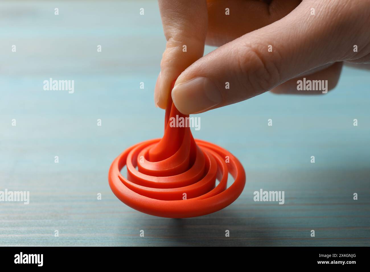 Woman playing with red spinning top at light blue wooden table, closeup ...