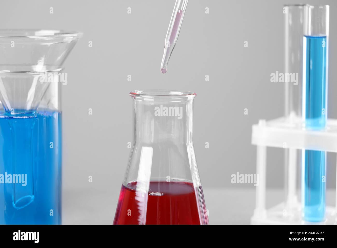 Dripping liquid from pipette into flask on grey background, closeup ...