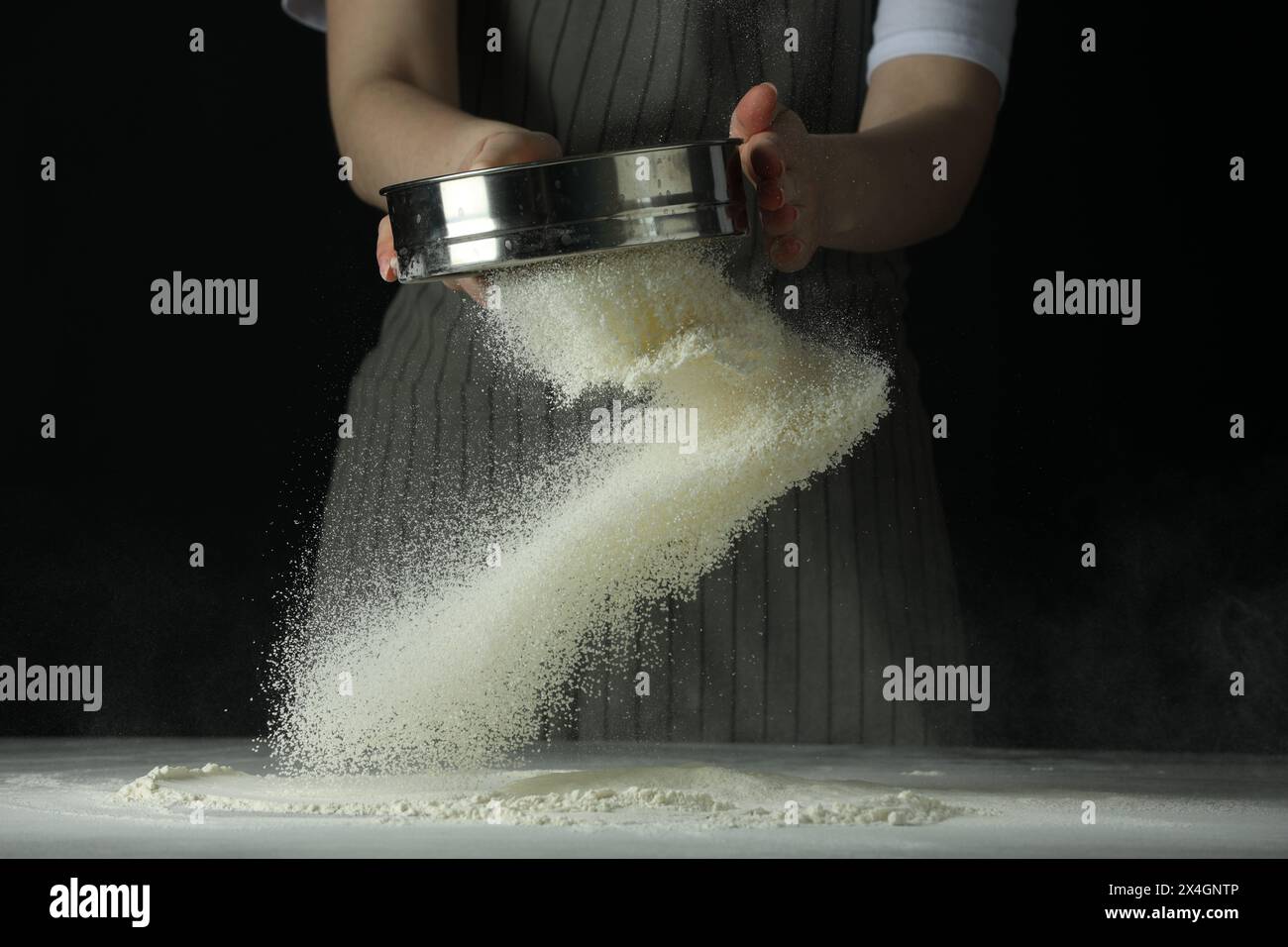 Woman sieving flour at table against black background, closeup Stock ...