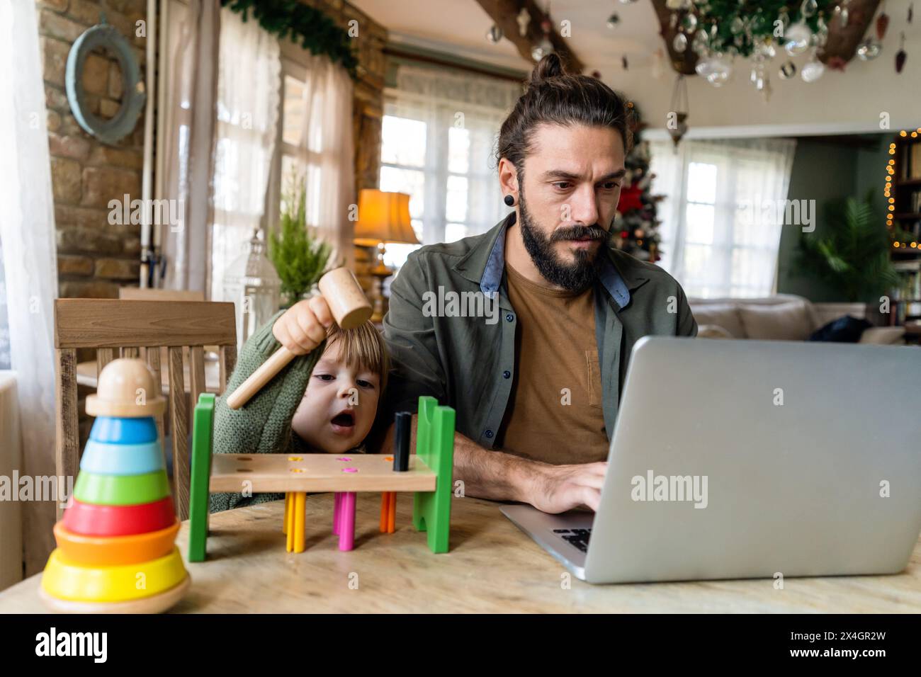 Multi-tasking freelance and fatherhood concept. Working single father with child and laptop ...