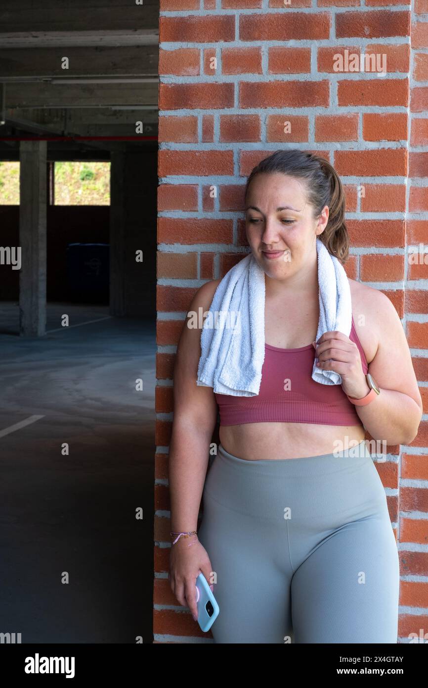 A curvy woman exhibits post-workout bliss, leaning against a brick ...