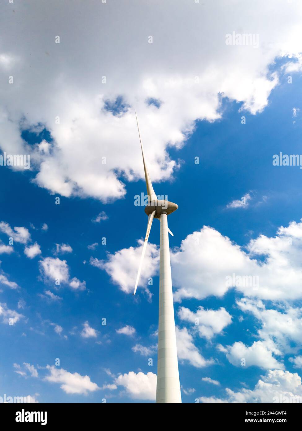 A tall wind turbine gracefully spins in the center of a clear, blue sky ...