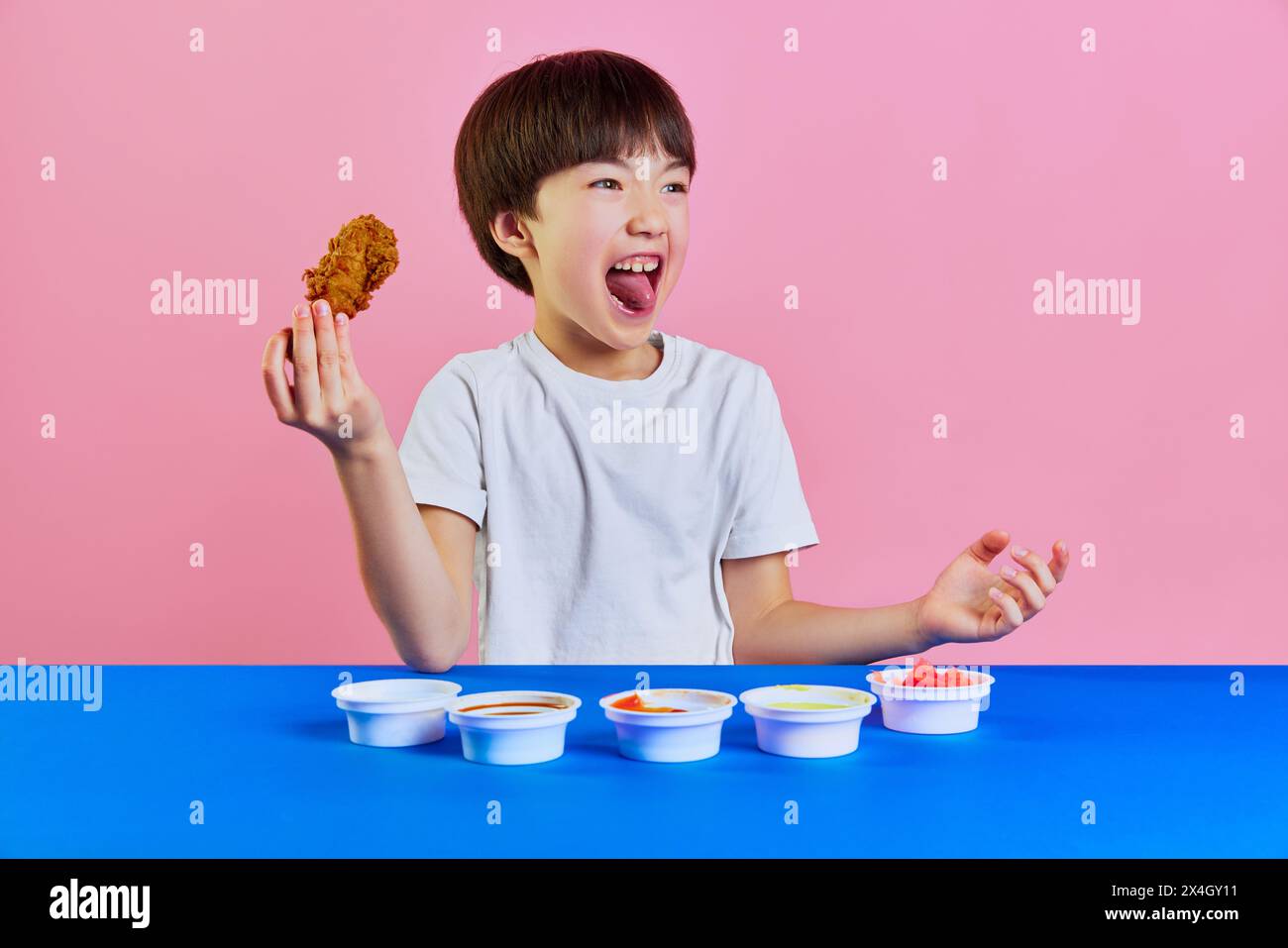 Emotional little Korean boy in white t-shirt eating spicy chicken ...