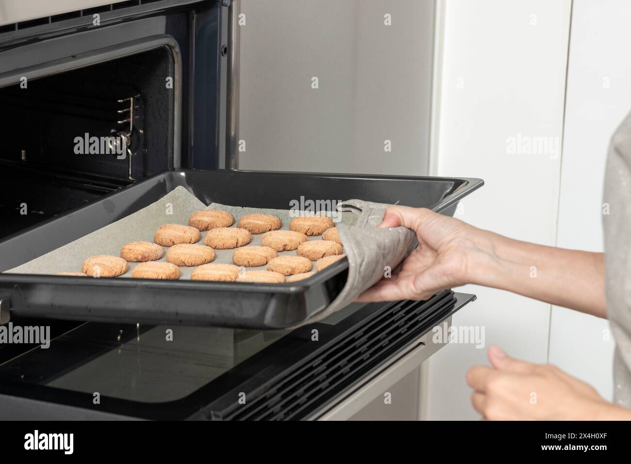 person pulling a tray of freshly baked cookies from an oven, using a ...