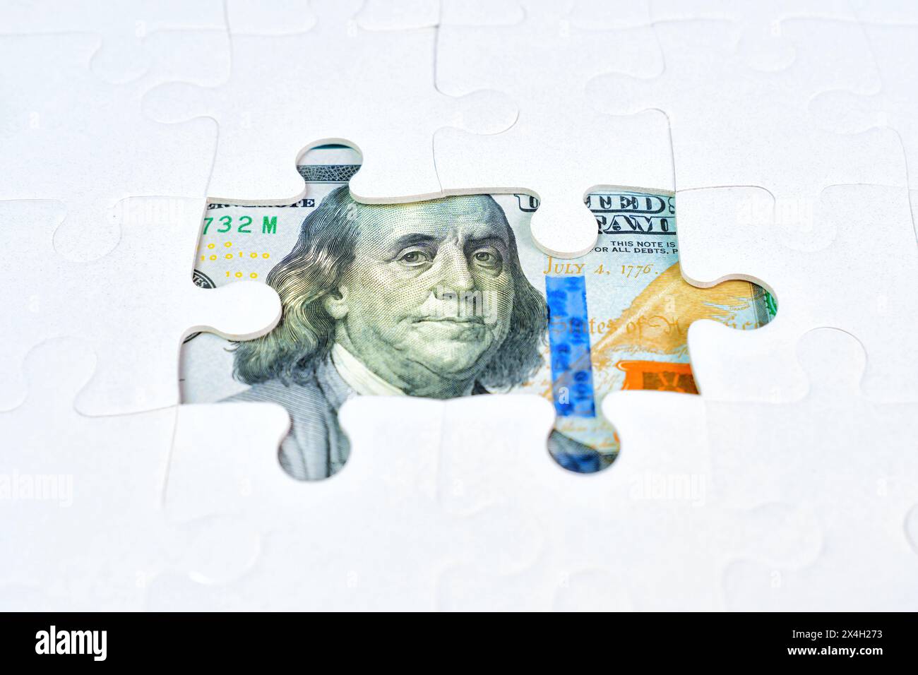 One hundred dollar bill elements seen through the openings in a jigsaw ...