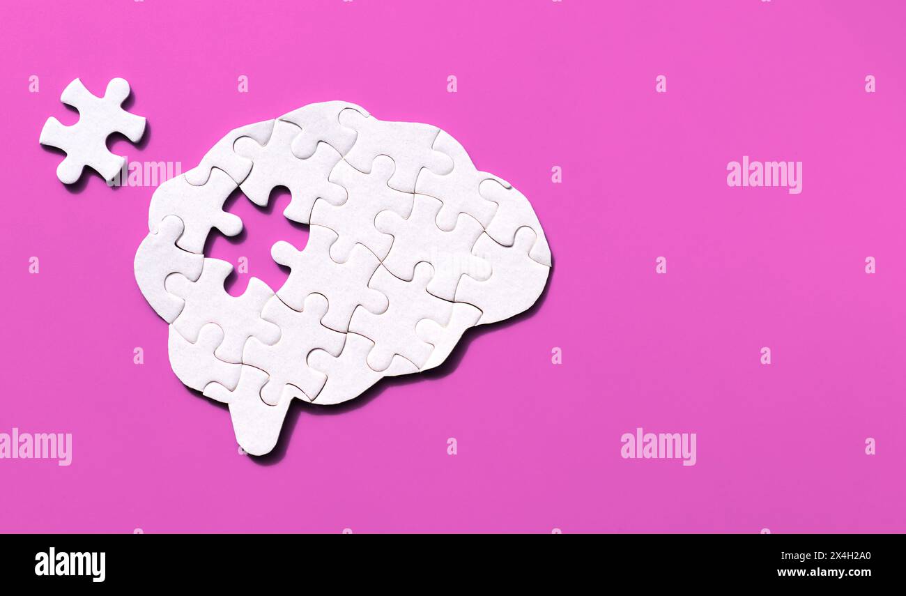 Brain-shaped puzzle with a missing element arranged on a soft pink ...