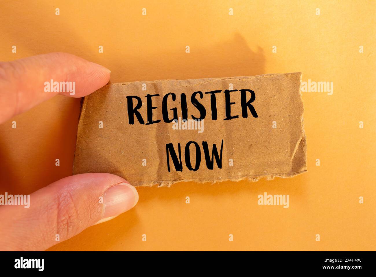 Register now words written on ripped cardboard paper piece with orange ...