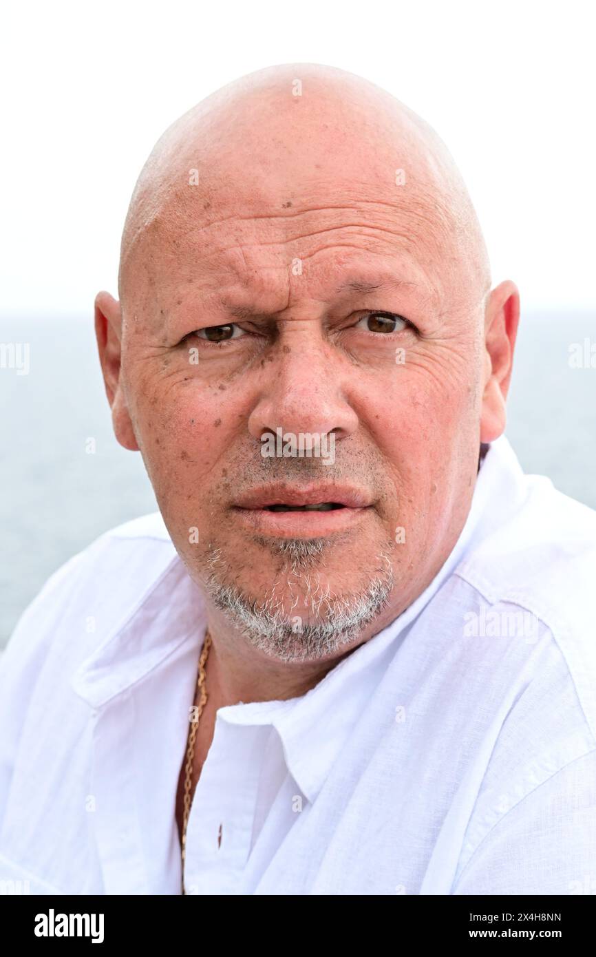 portrait of a bald man in a white shirt, by the sea, expressing ...