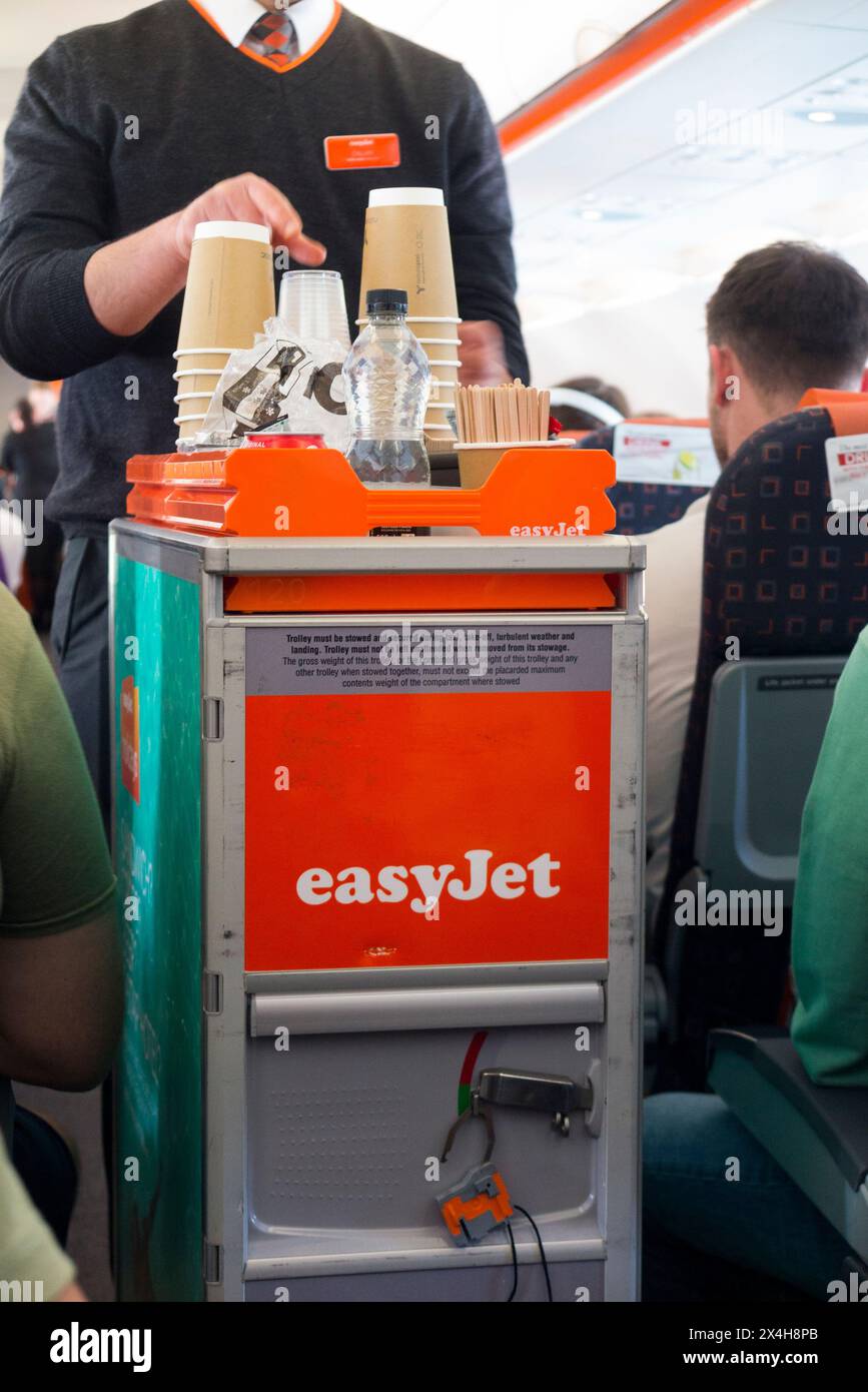 Cabin crew / air steward serves drinks and snacks to passengers from a ...